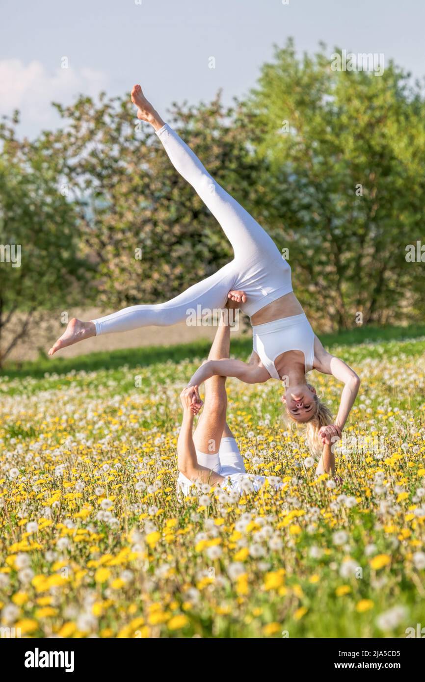 Beautiful young couple doing acro yoga in park. Man lying on grass and ...