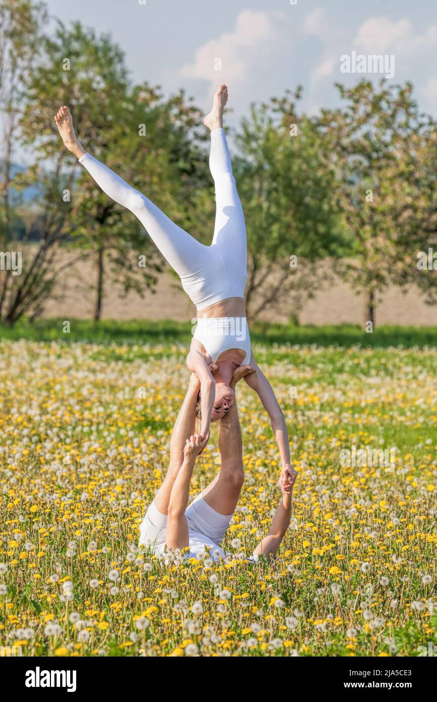Beautiful young couple doing acro yoga in park. Man lying on grass and ...