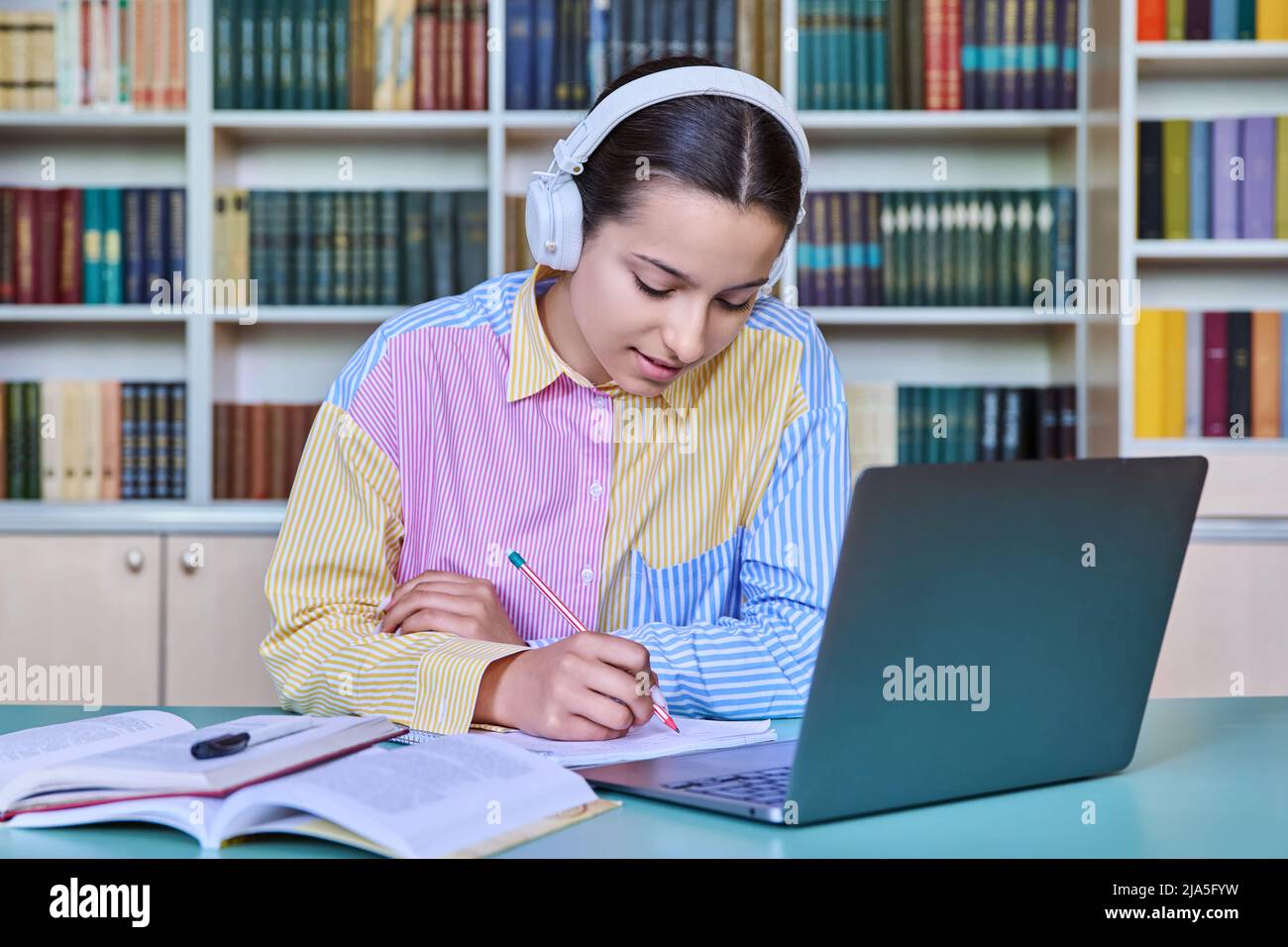 High school student girl in headphones studying in school library using ...