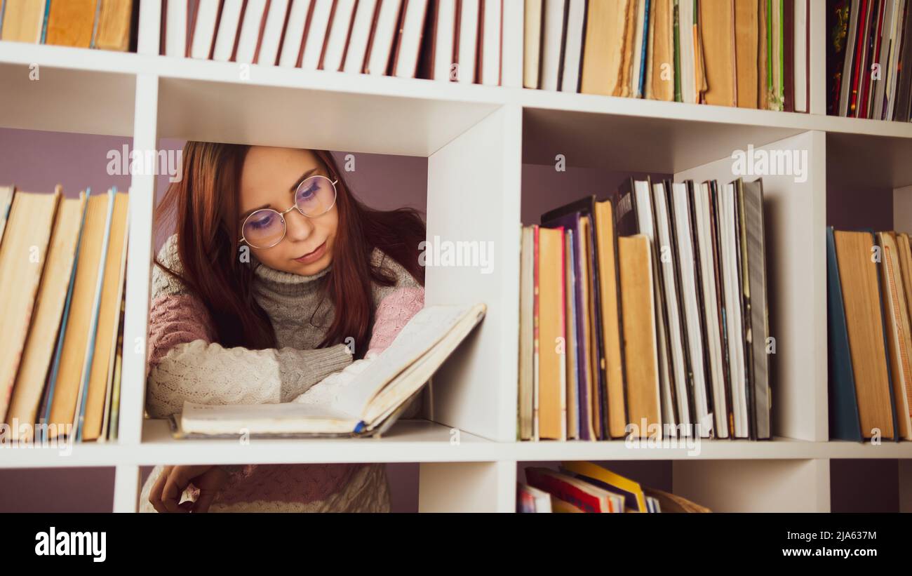A student is reading a book in the library behind the bookshelves. A ...