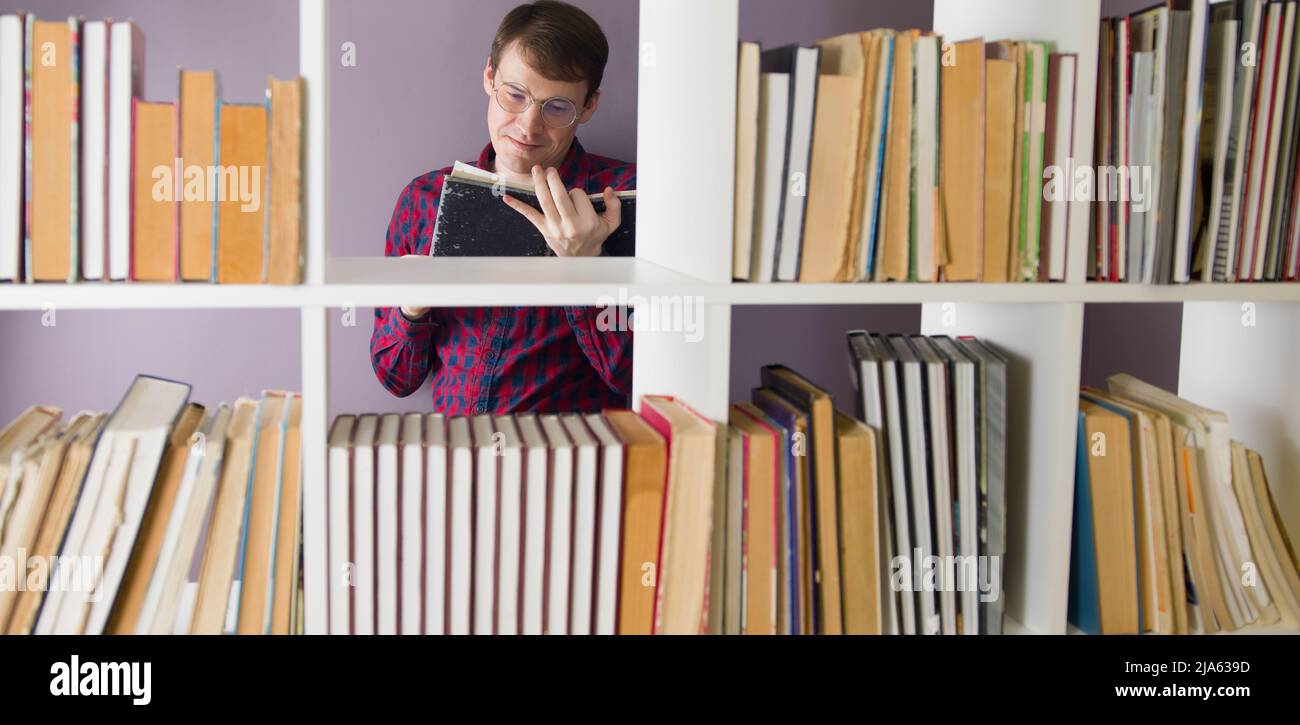 A man is reading a book in the library behind the bookshelves. A ...