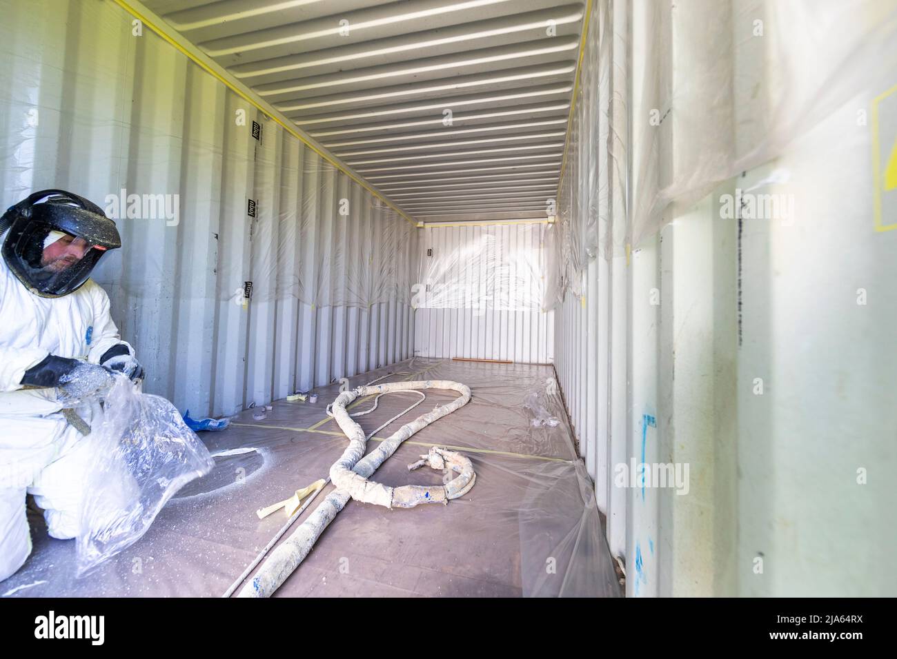 A workman sprays a shipping container ceiling with Grapho Therm to ...