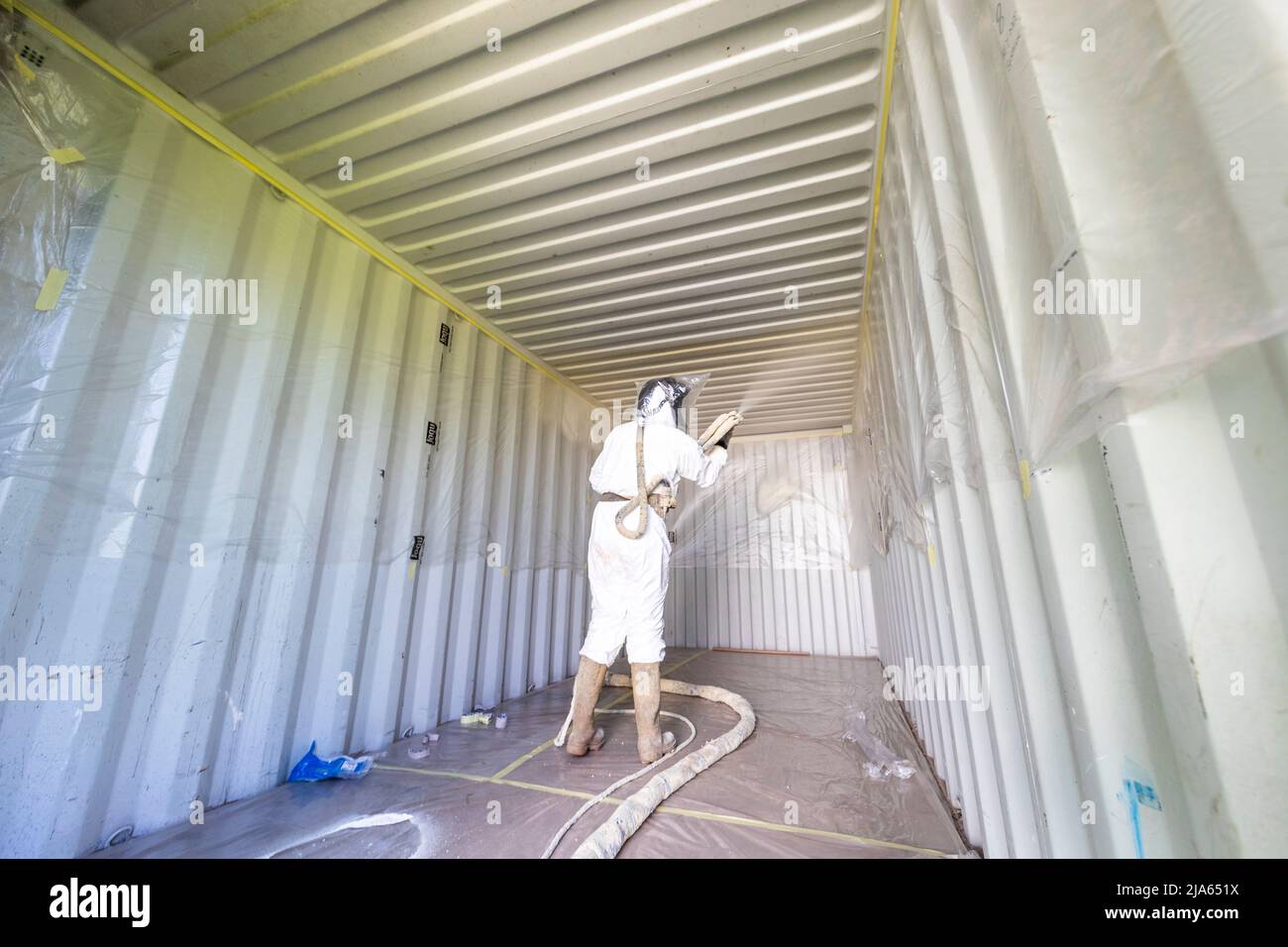 A workman sprays a shipping container ceiling with Grapho Therm to ...