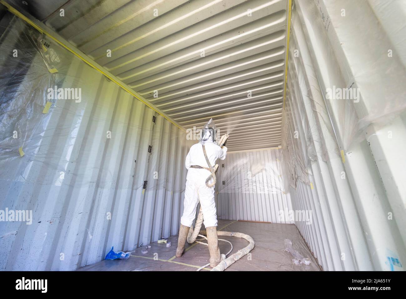 A workman sprays a shipping container ceiling with Grapho Therm to ...