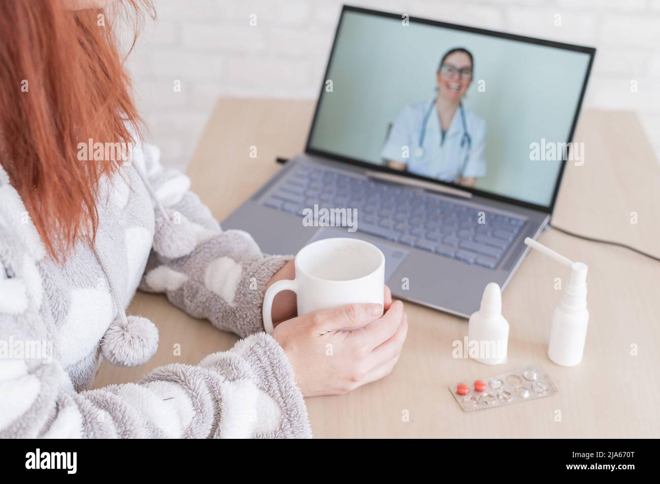 A woman with a cold is on sick leave and is looking at a laptop video ...