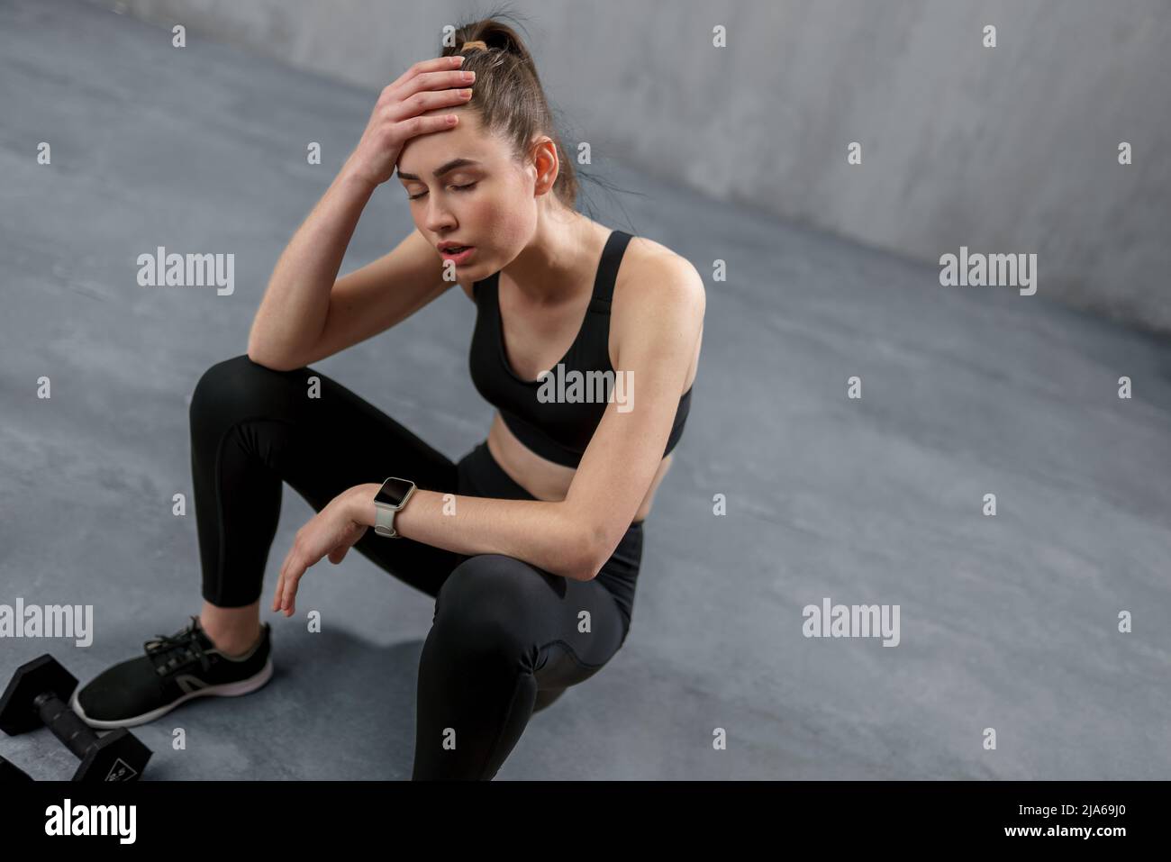 Tired young sporty woman having rest after workout, sitting on floor at ...