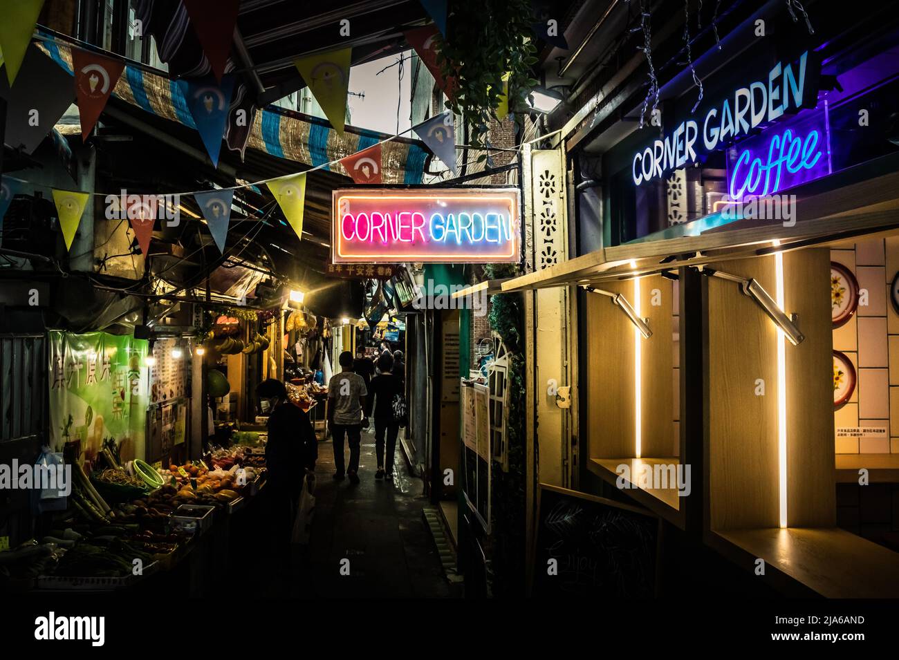Colourful neon signs light up a dark alley with market stalls and a ...