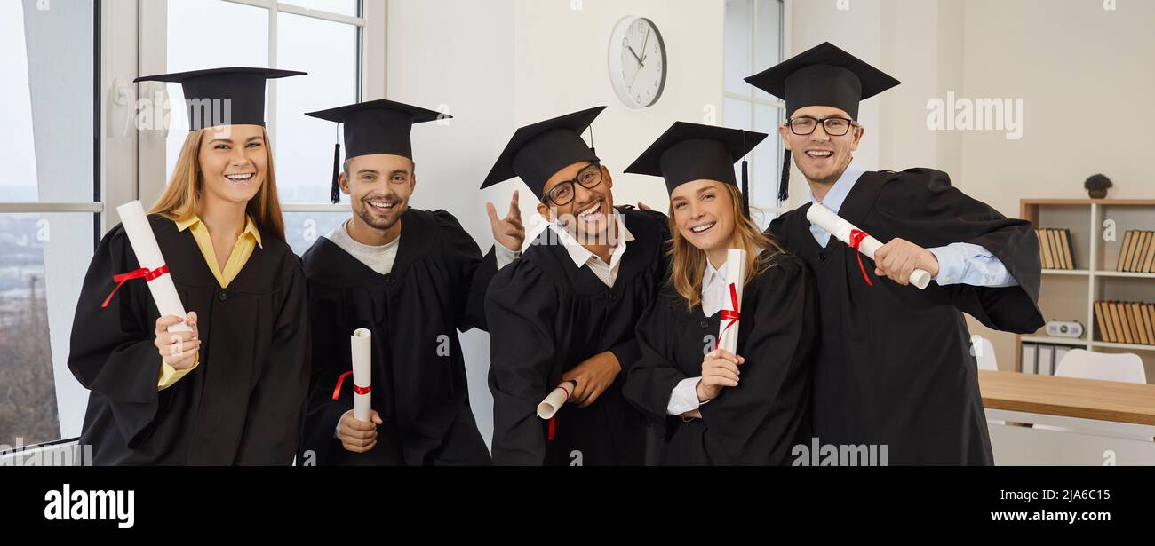 Happy, joyful university graduates in caps and gowns holding diplomas ...