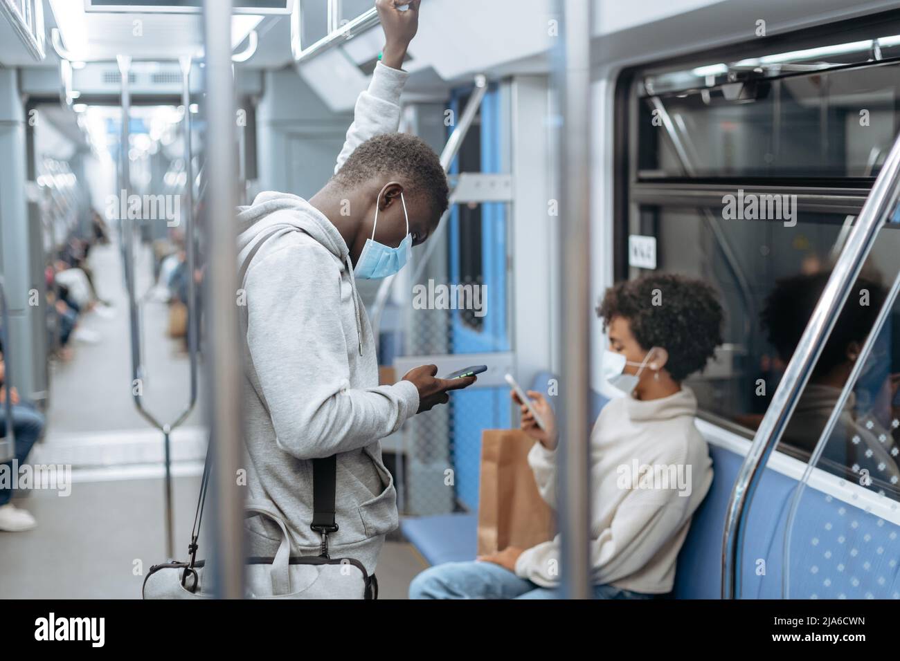 passengers in protective masks using their devices in the subway car ...