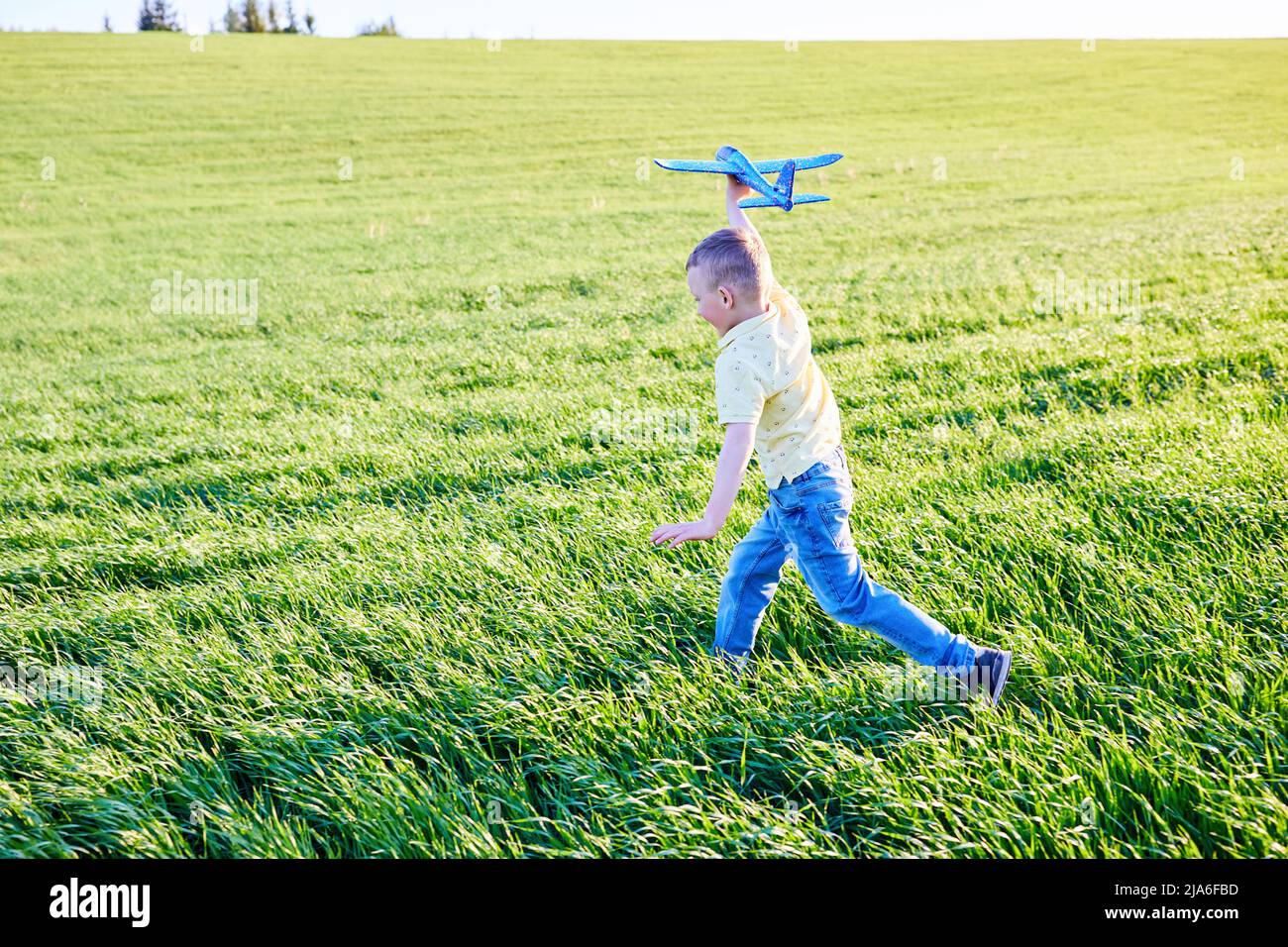 Boy runs with toy airplane in summer through field. Happy child running ...