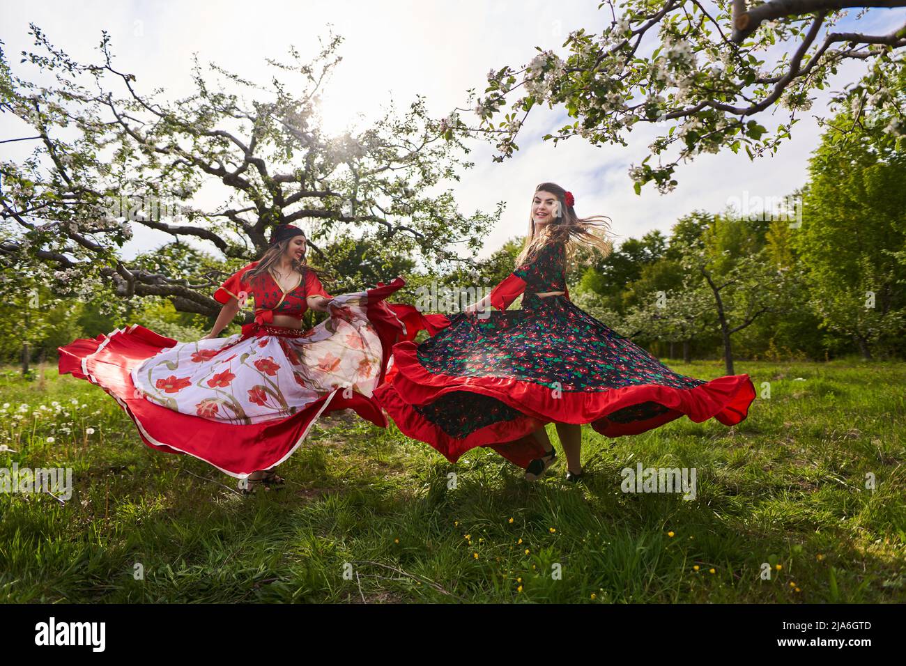 Two young women in traditional gypsy costume dancing in a flowering ...