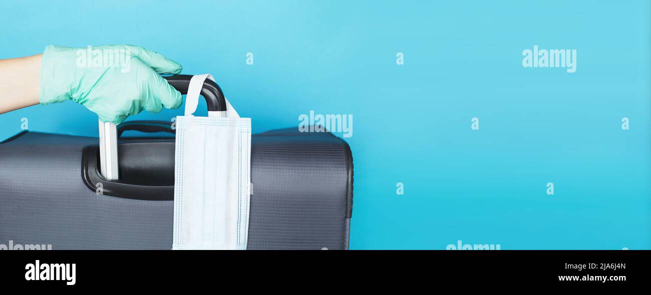 Hand with a luggage bag and medical mask isolated on a blue background ...