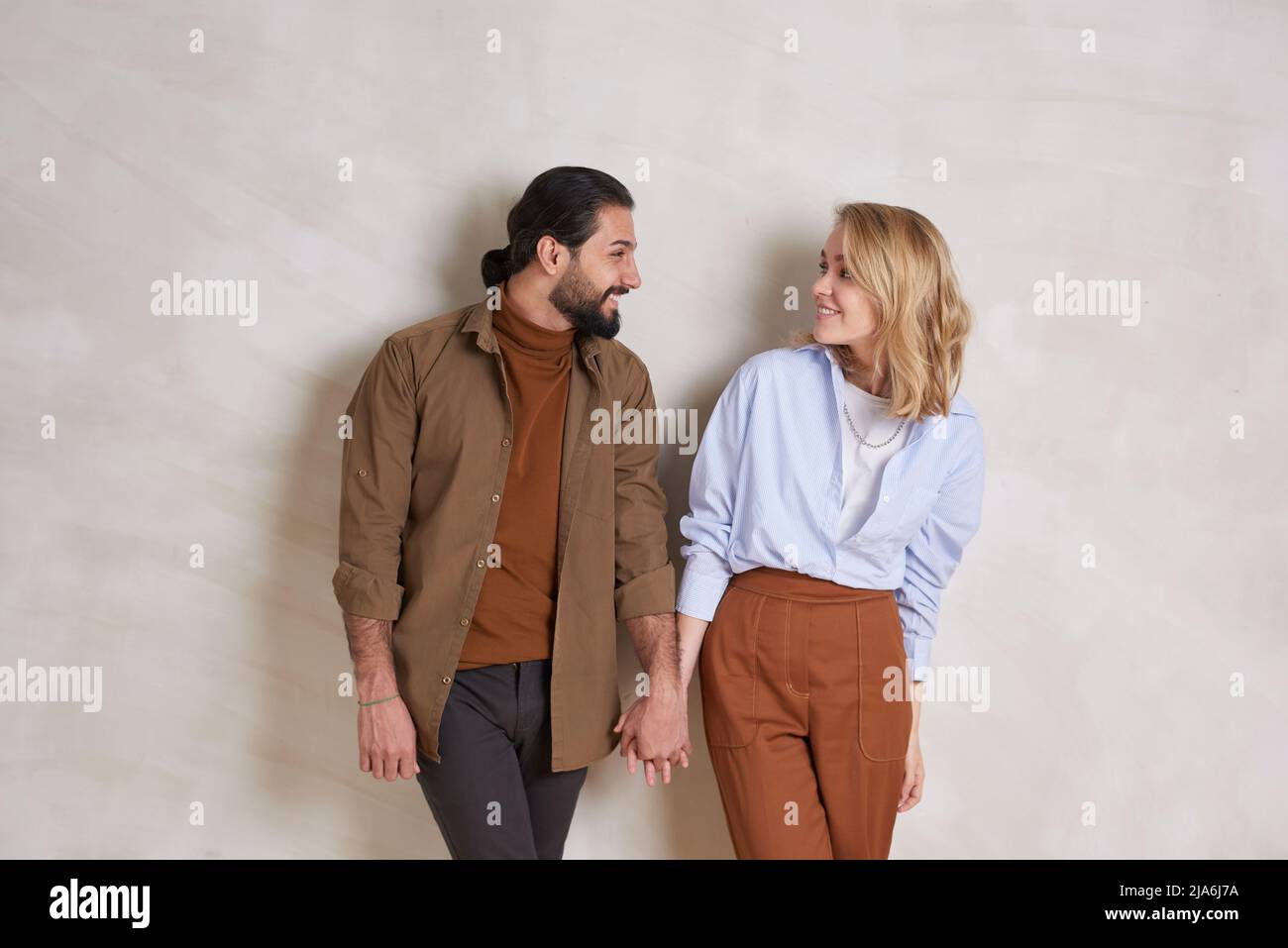 Medium long portrait of lovely young couple standing against wall ...