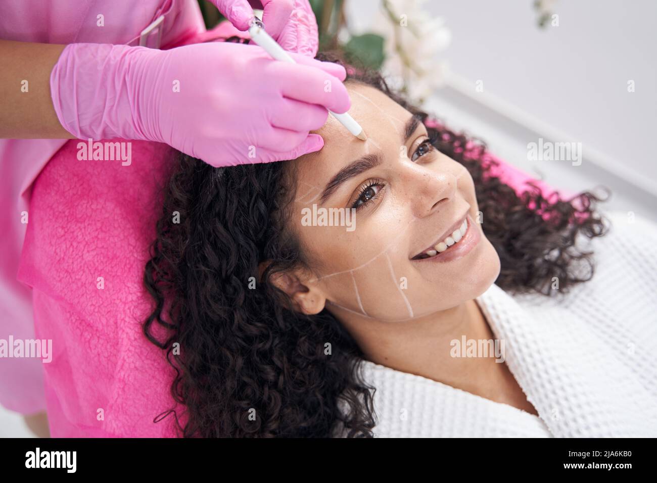 Happy young woman is given markings on forehead for beauty procedure ...