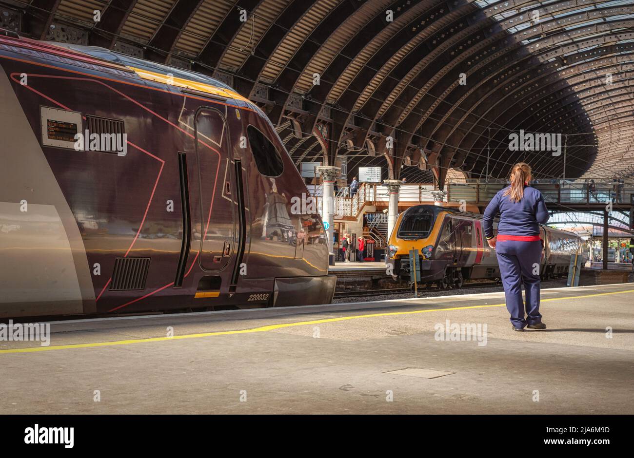 A locomotive stands at a railway station platform and a crew member is ...