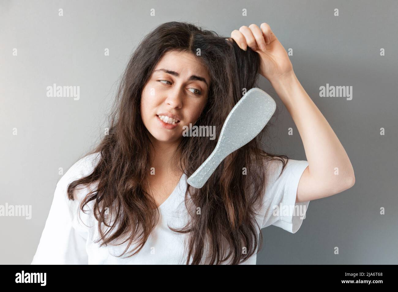 Portrait of young confused woman holds a tangled strand of her hair ...