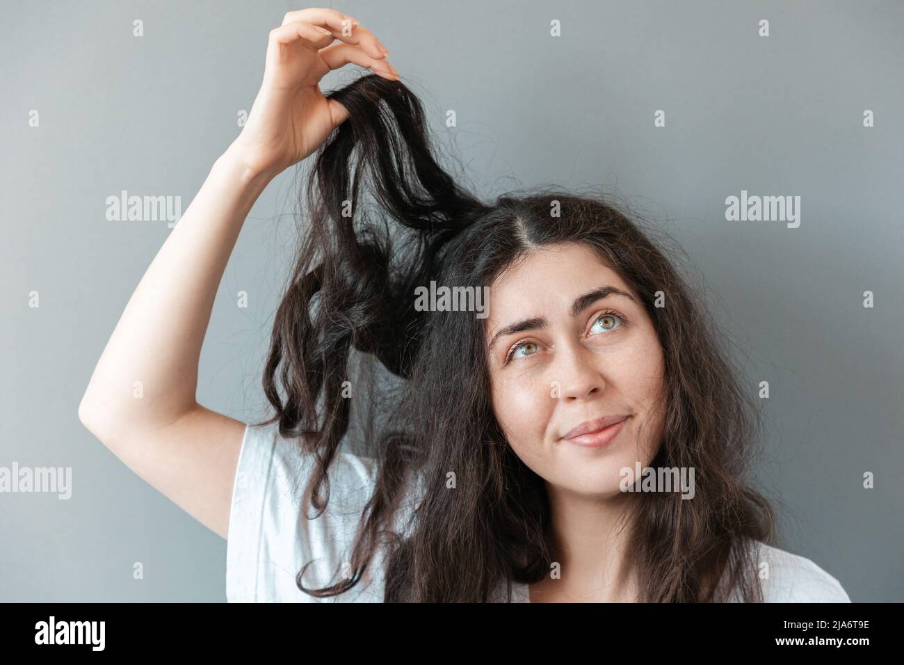 Young upset woman holds a tangled strand of her hair in bewilderment ...