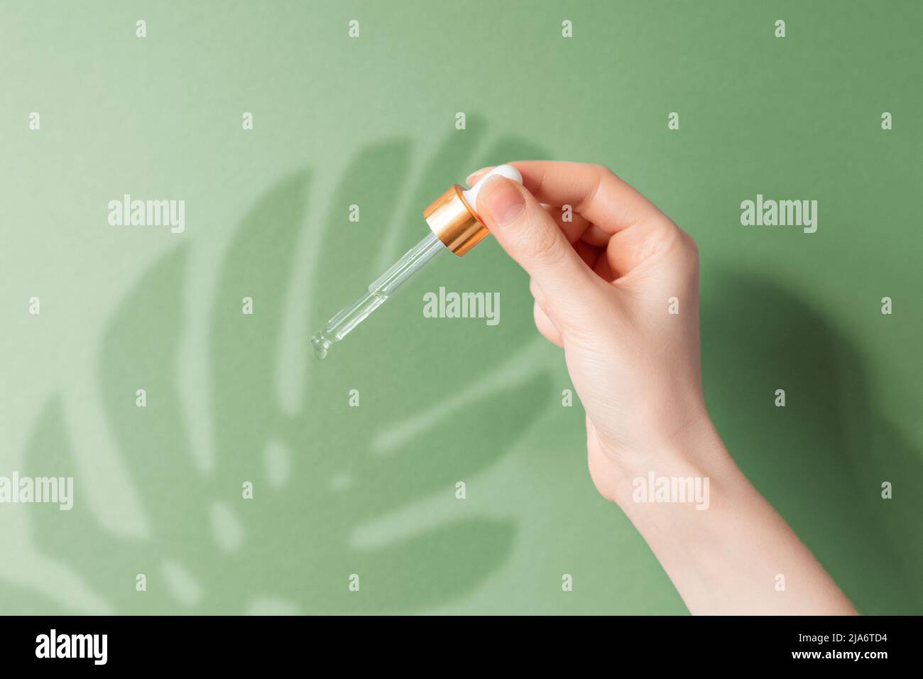 A female's hand holds a pipette with cosmetic oil for skin care. Green ...