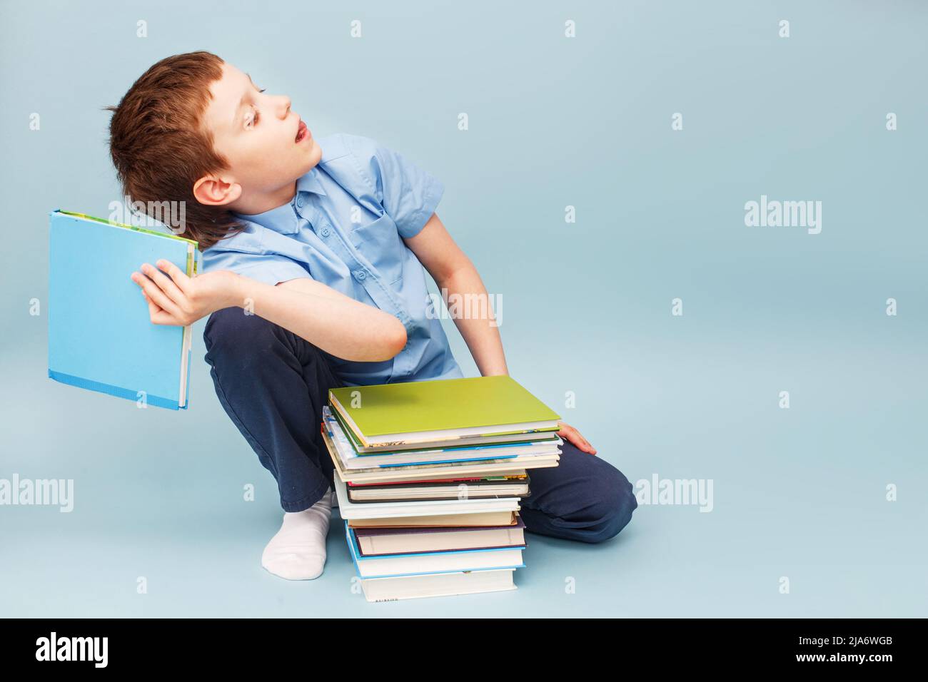 Upset schoolboy sitting with pile of school books and throwing a ...