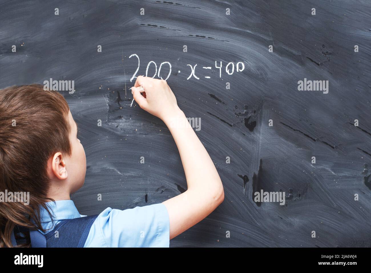 Boy standing back in front of a school blackboard and writing ...