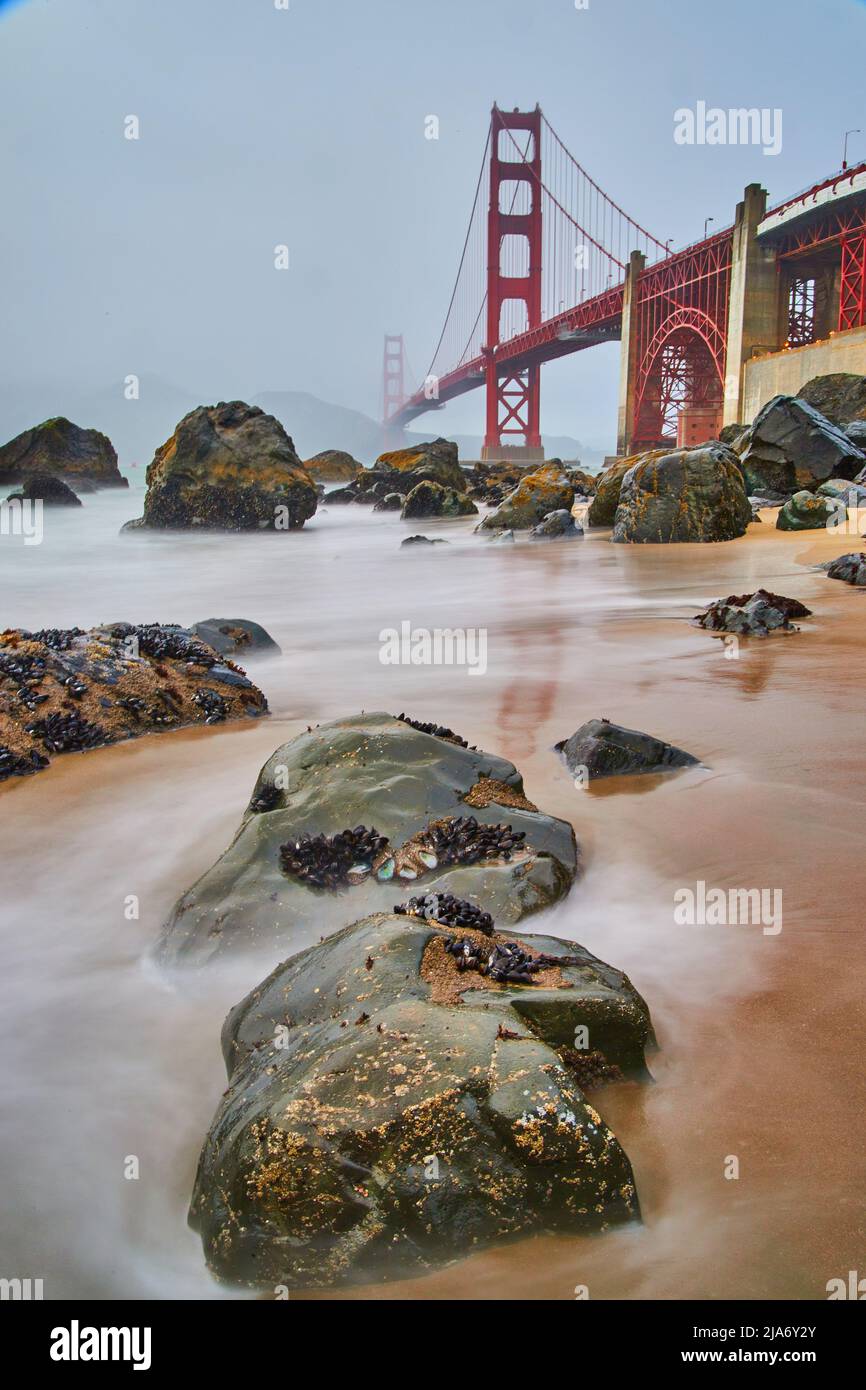 Golden Gate Bridge on foggy morning with smooth waves over tide pools ...