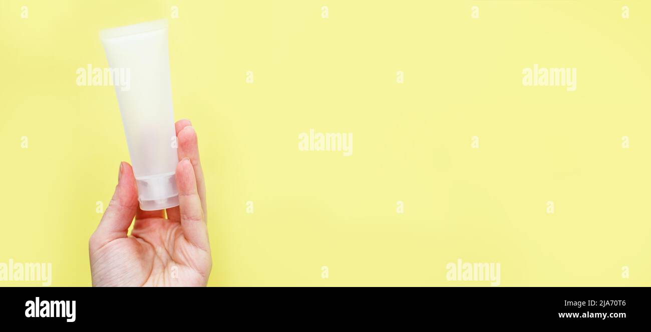 Female hand holding cream tube cosmetic products on a yellow background ...