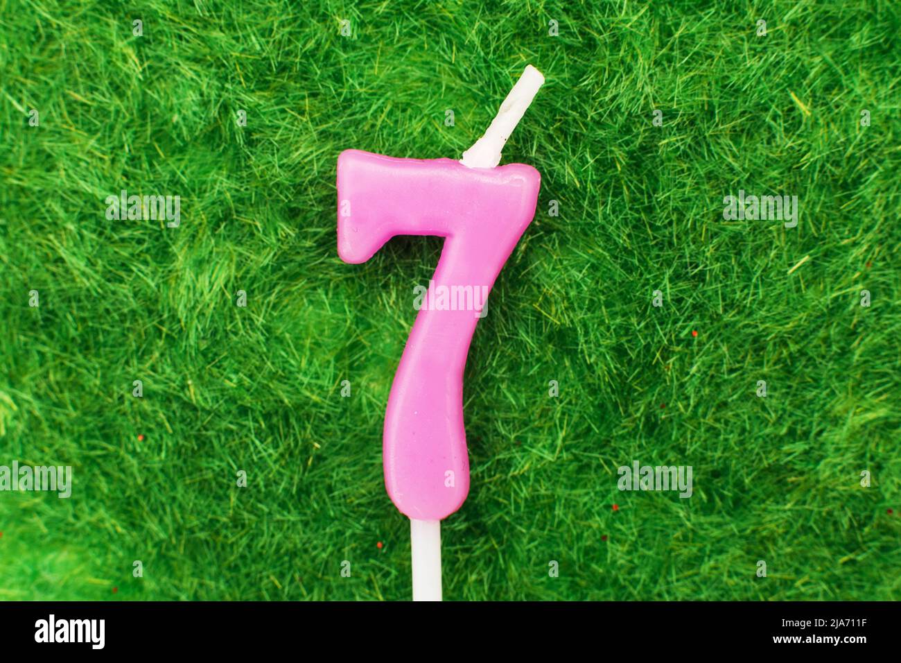candle in the form of number seven on the green grass background, a ...