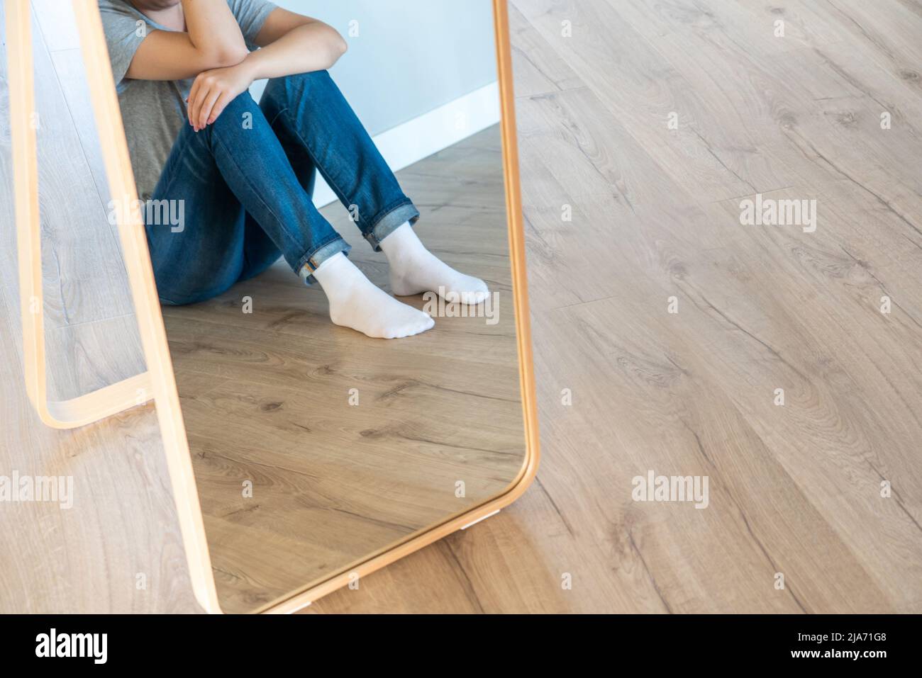 Reflection in mirrow of a sad woman sitting on a floor alone in empty ...