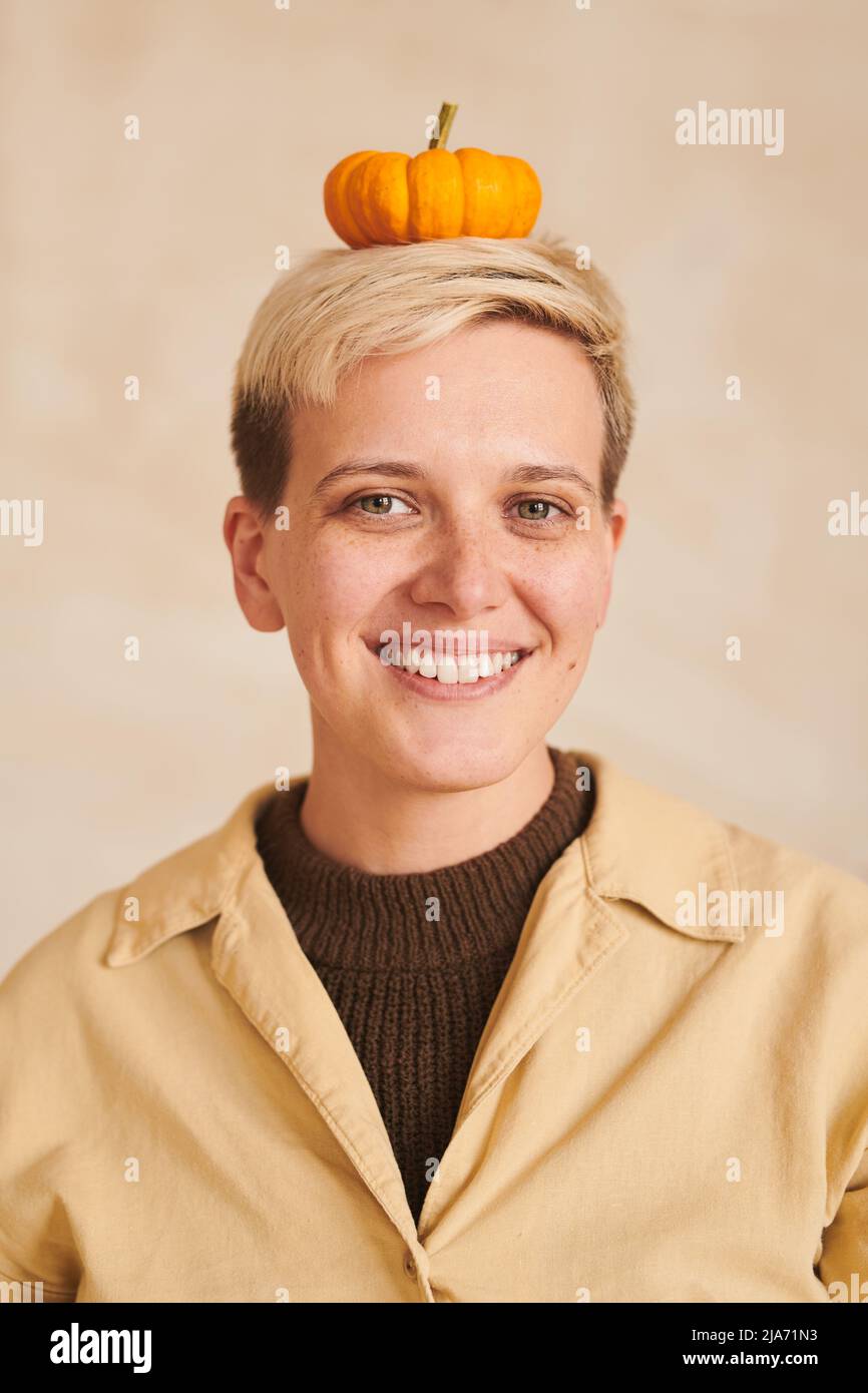 Portrait of smiling tomboy girl with short hair keeping small pumpkin ...