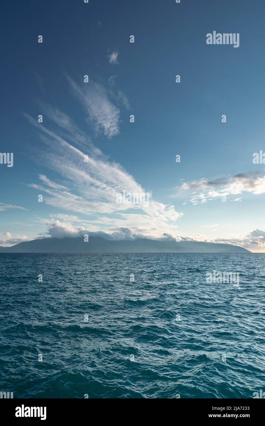 Bright blue ocean in a cloudy blue sky, with islands on the horizon in ...