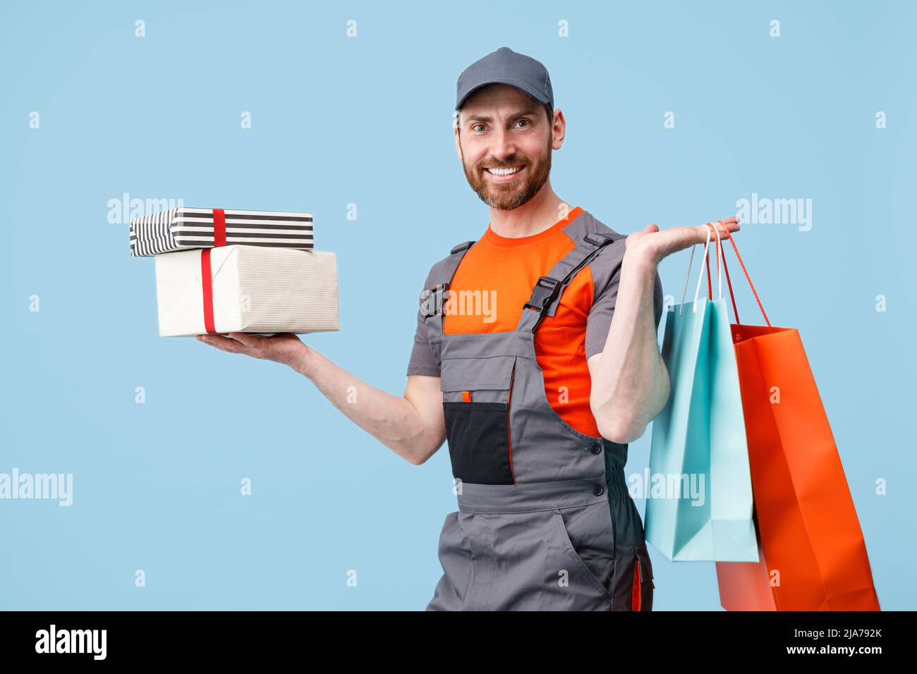 Delivery man in uniform holding shopping bags and gift boxes on blue ...