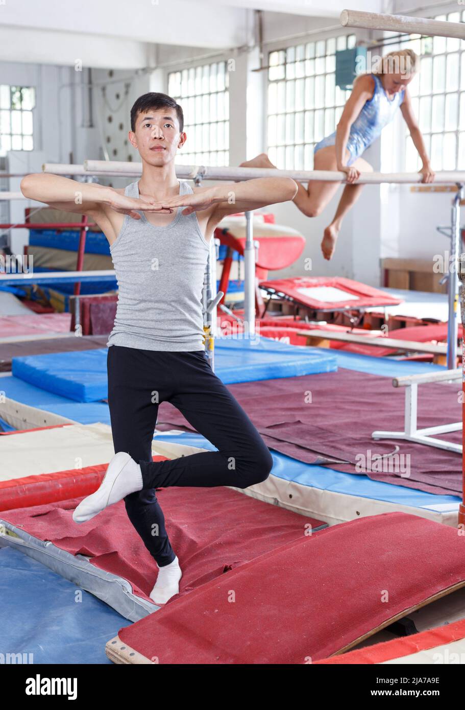 Sporty man asian gymnast during workout in gym, woman on background ...