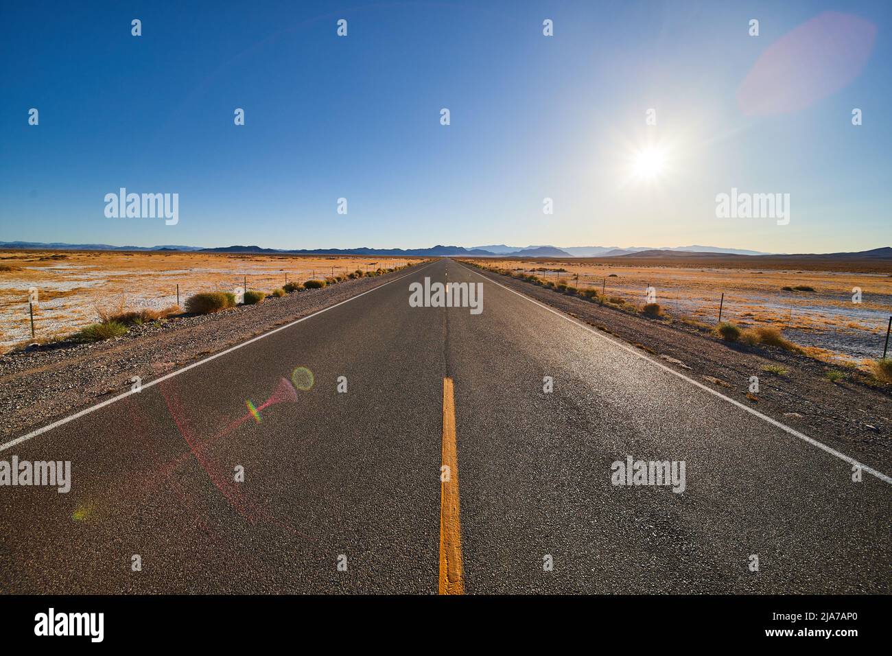 Desert paved road leading into endless desert with sun and blue sky ...