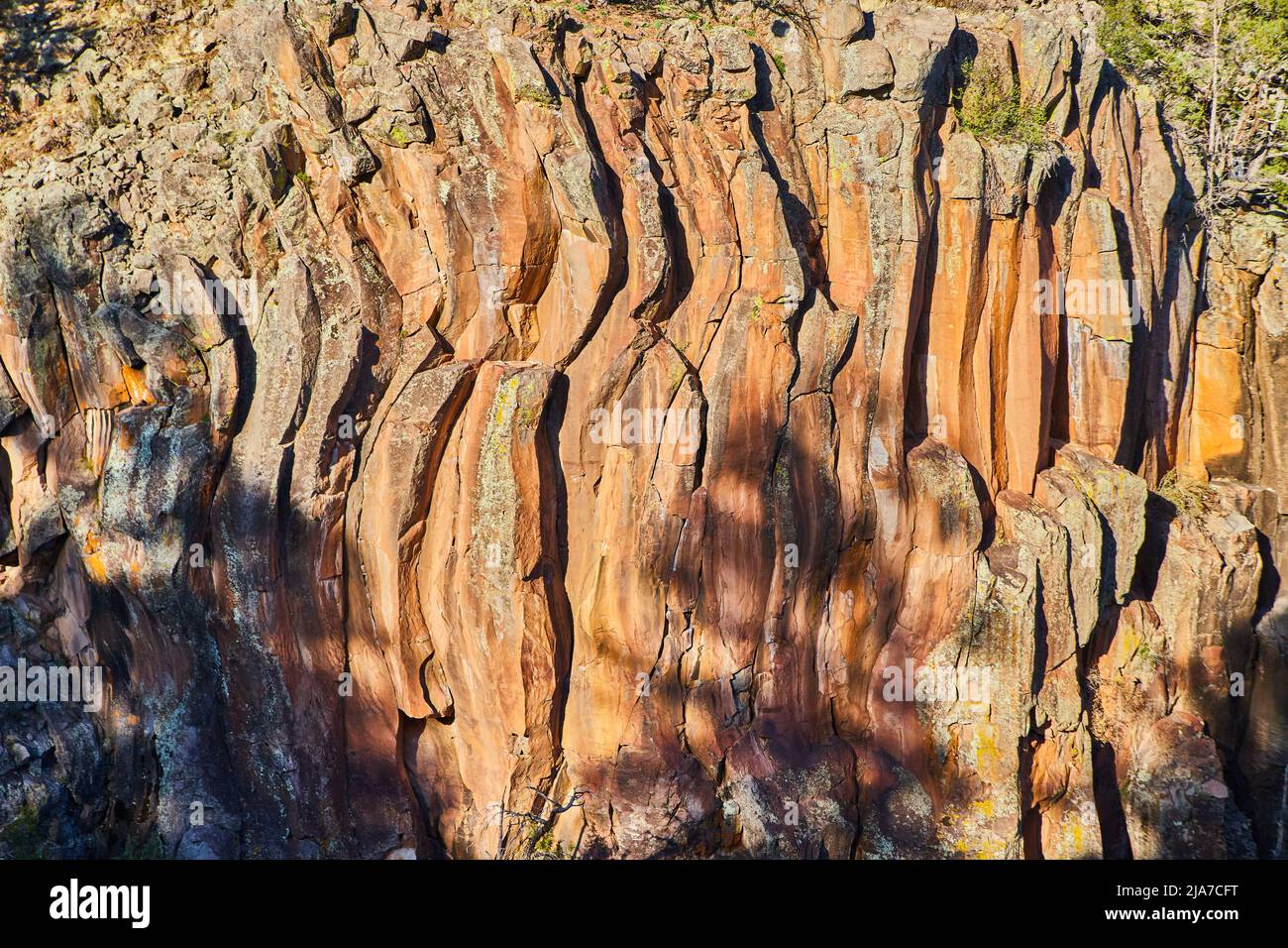 Detail of cliff with wavy vertical rock formations in golden light ...