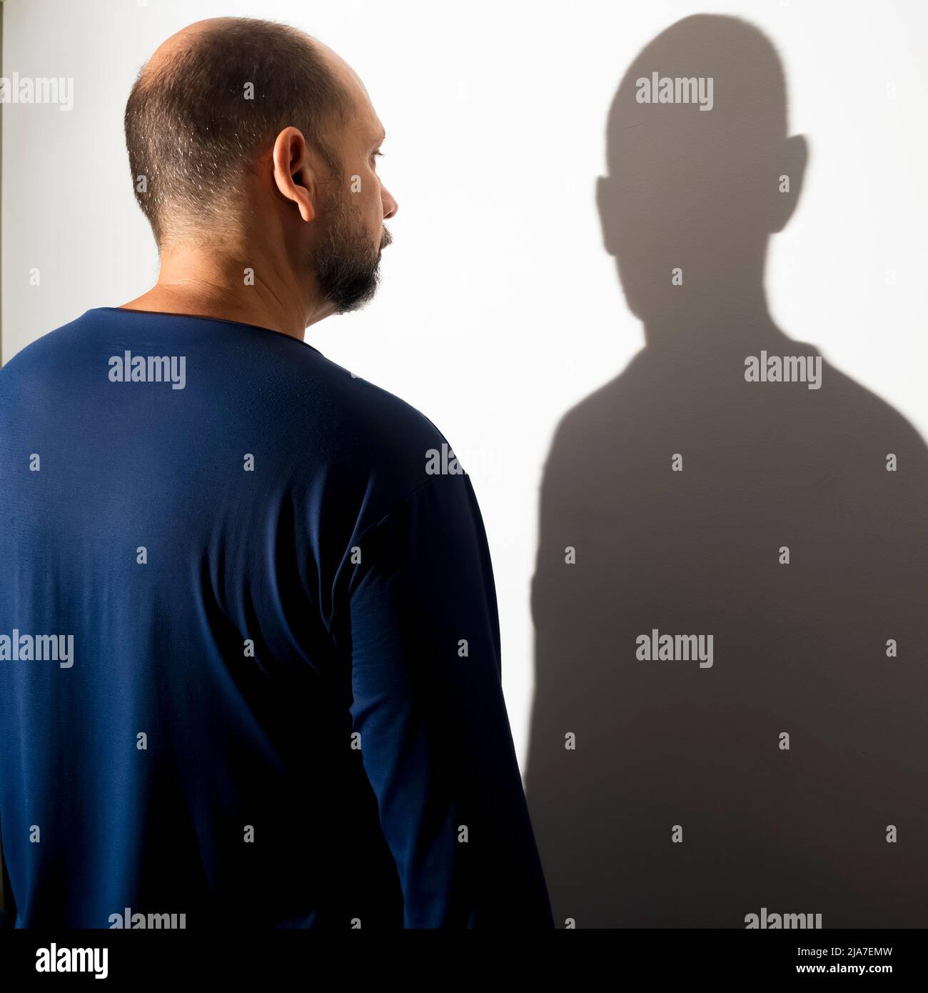 Portrait of a man and his shadow against white wall background ...