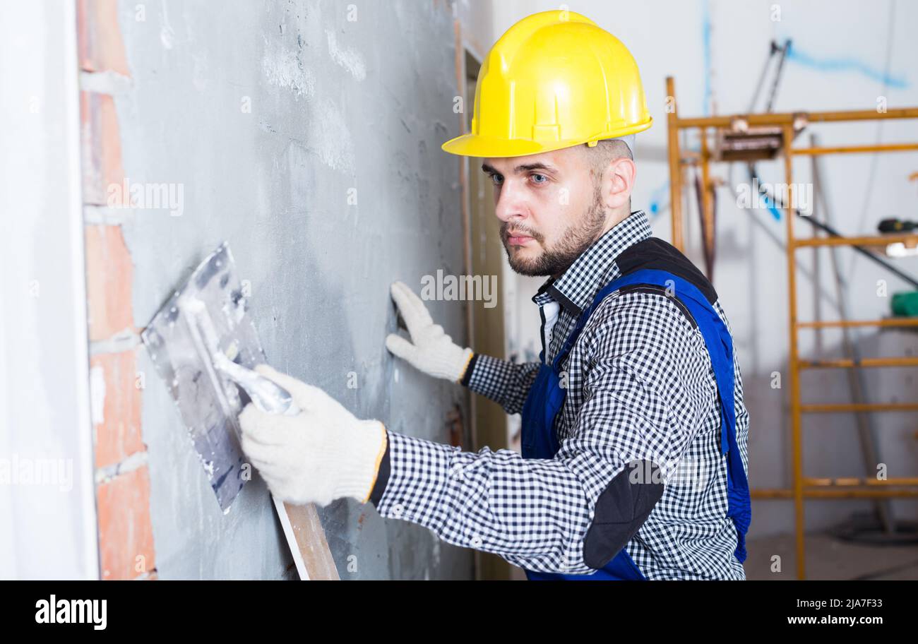 Smiling workman in the helmet is plastering the wall Stock Photo - Alamy