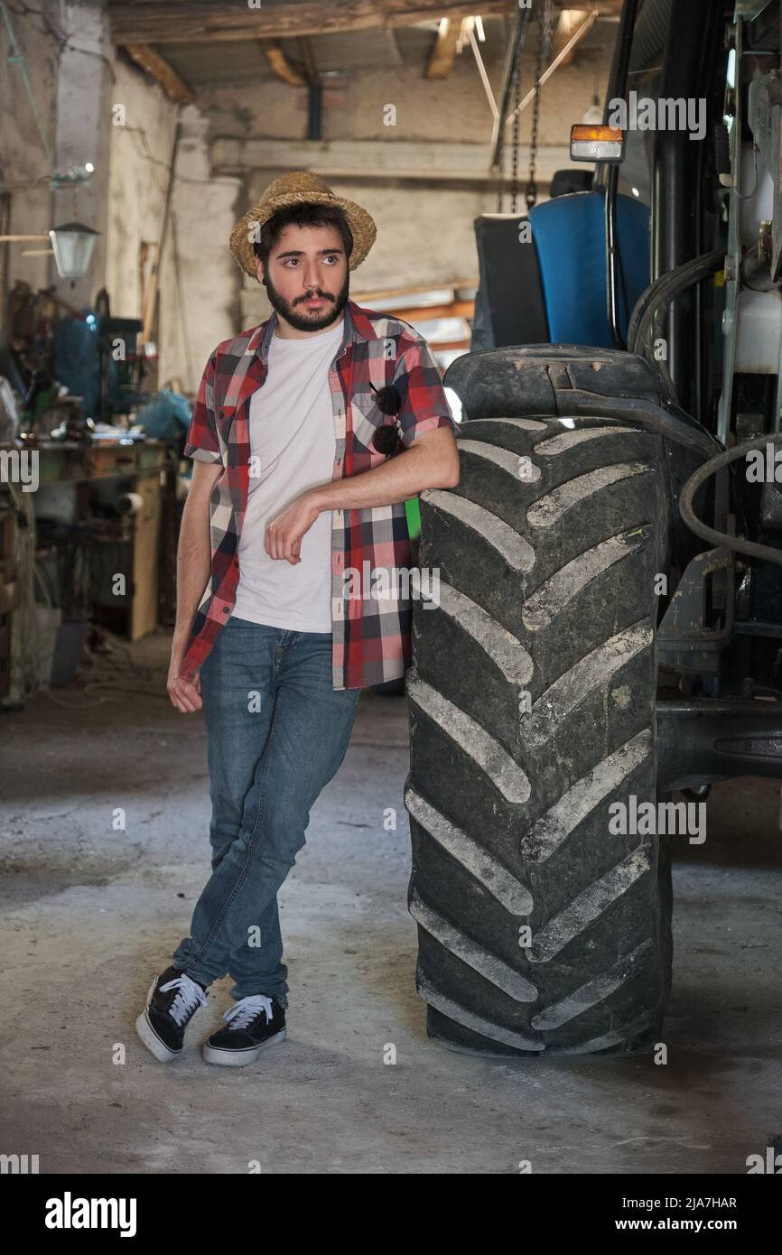 Young farmer leaning on tractor wheel in a barn Stock Photo - Alamy