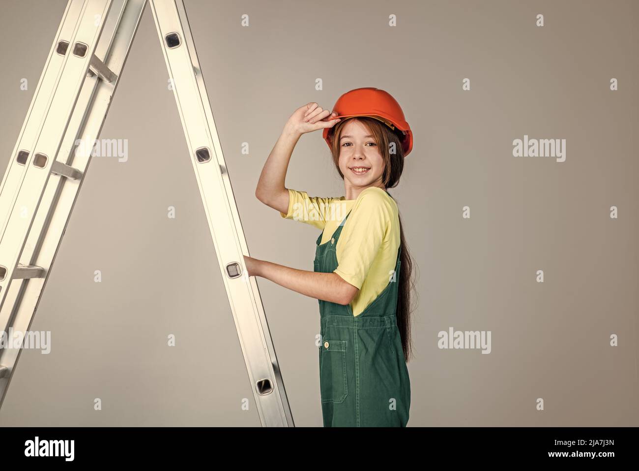 teen girl in uniform and helmet with ladder. female builder in hard hat ...