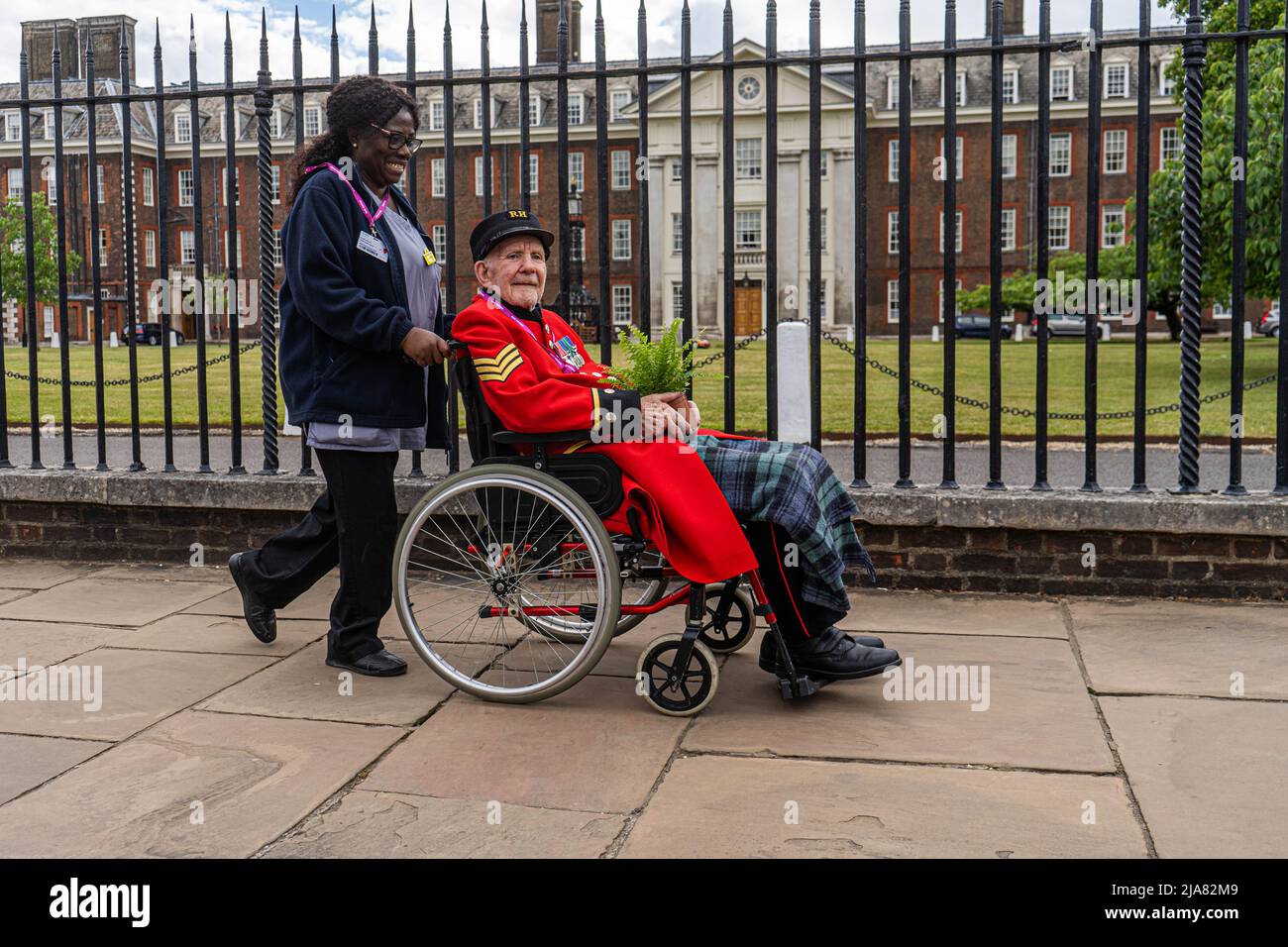 London UK, 28 May 2022. A Royal Chelsea pensioner in a wheelchair carry ...