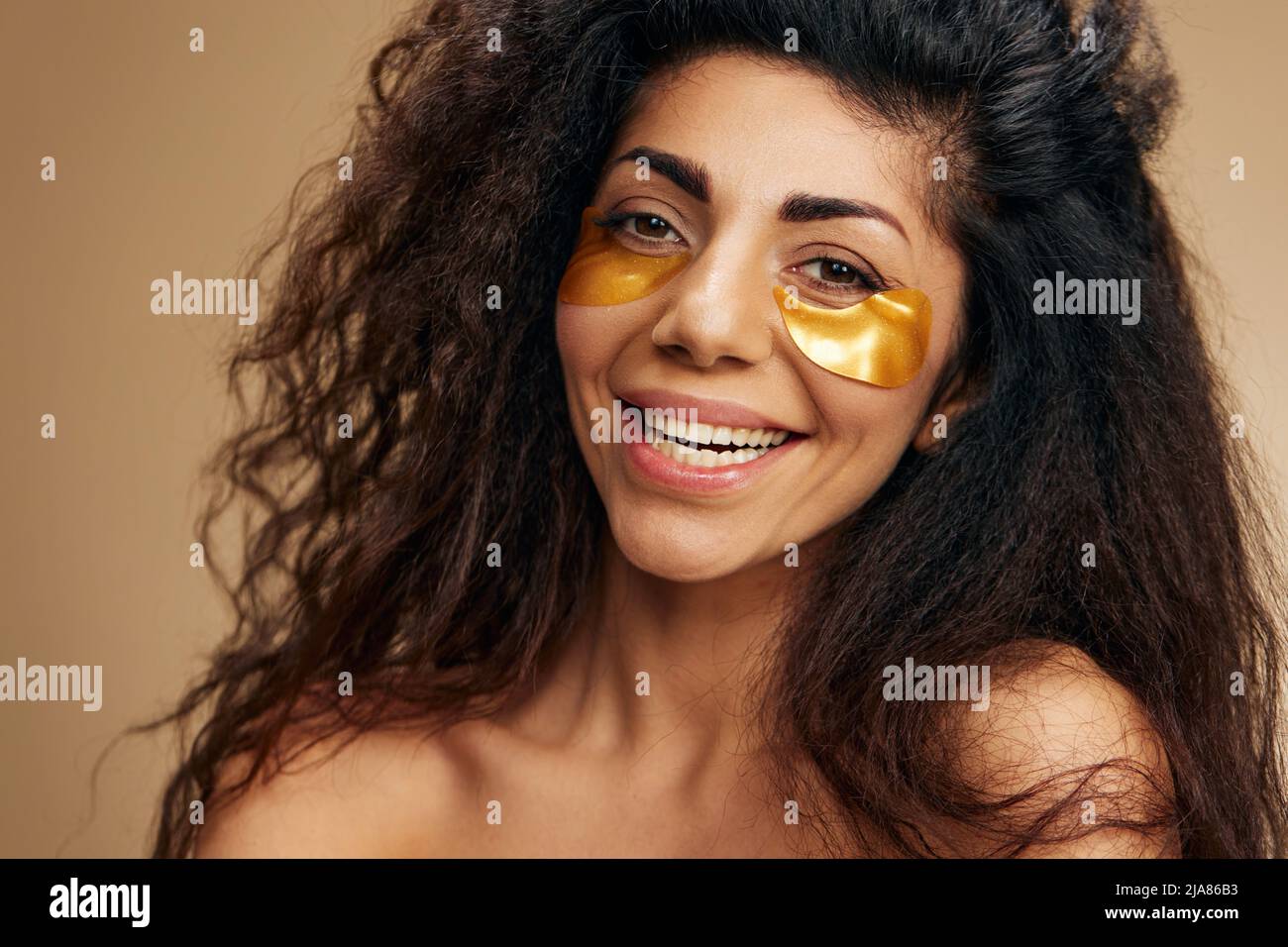 Happy attractive Latin woman with gold hydrogel patches under eye smile ...