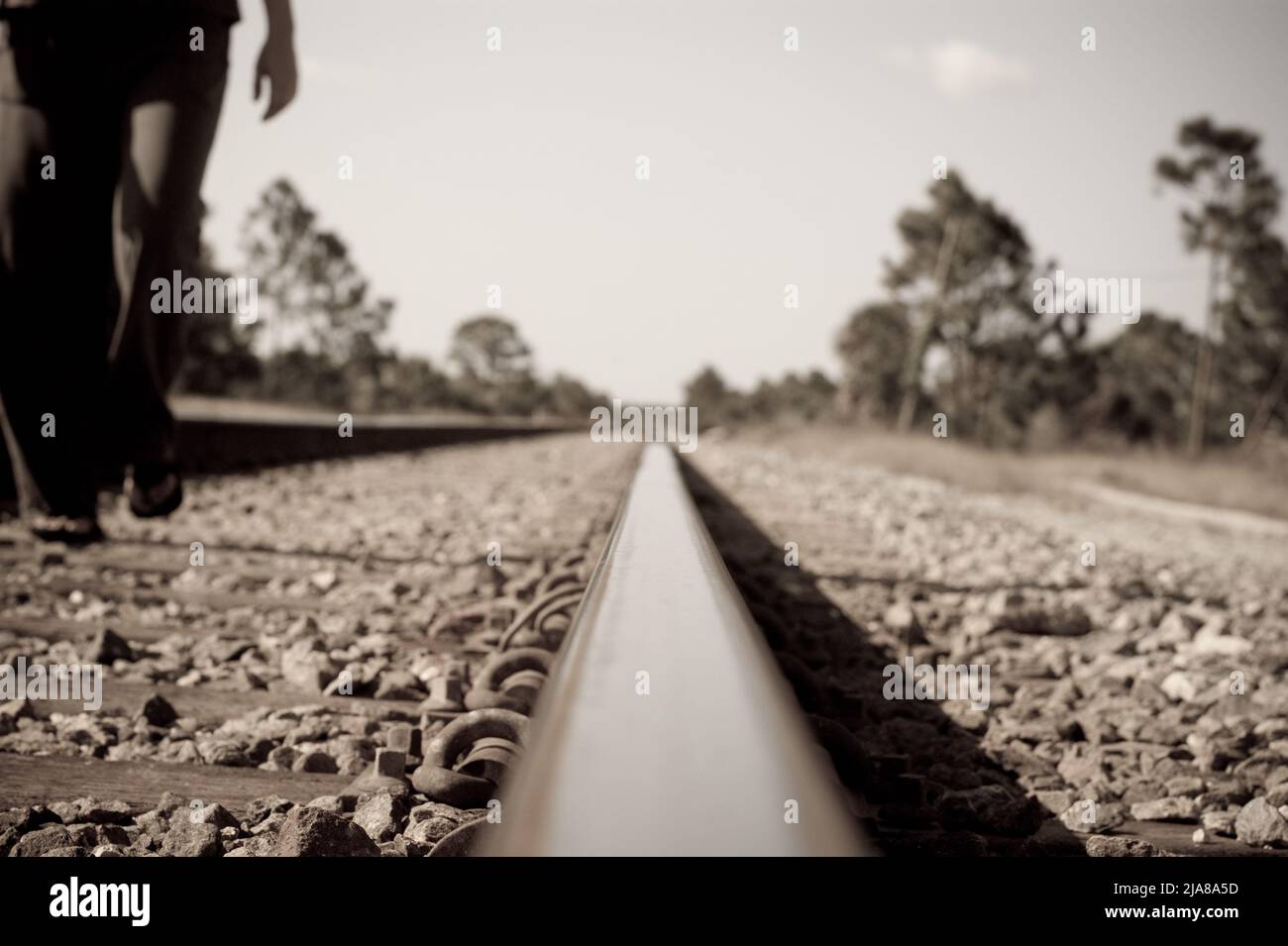 The legs and hand of a woman as she walks along a railroad track out in ...