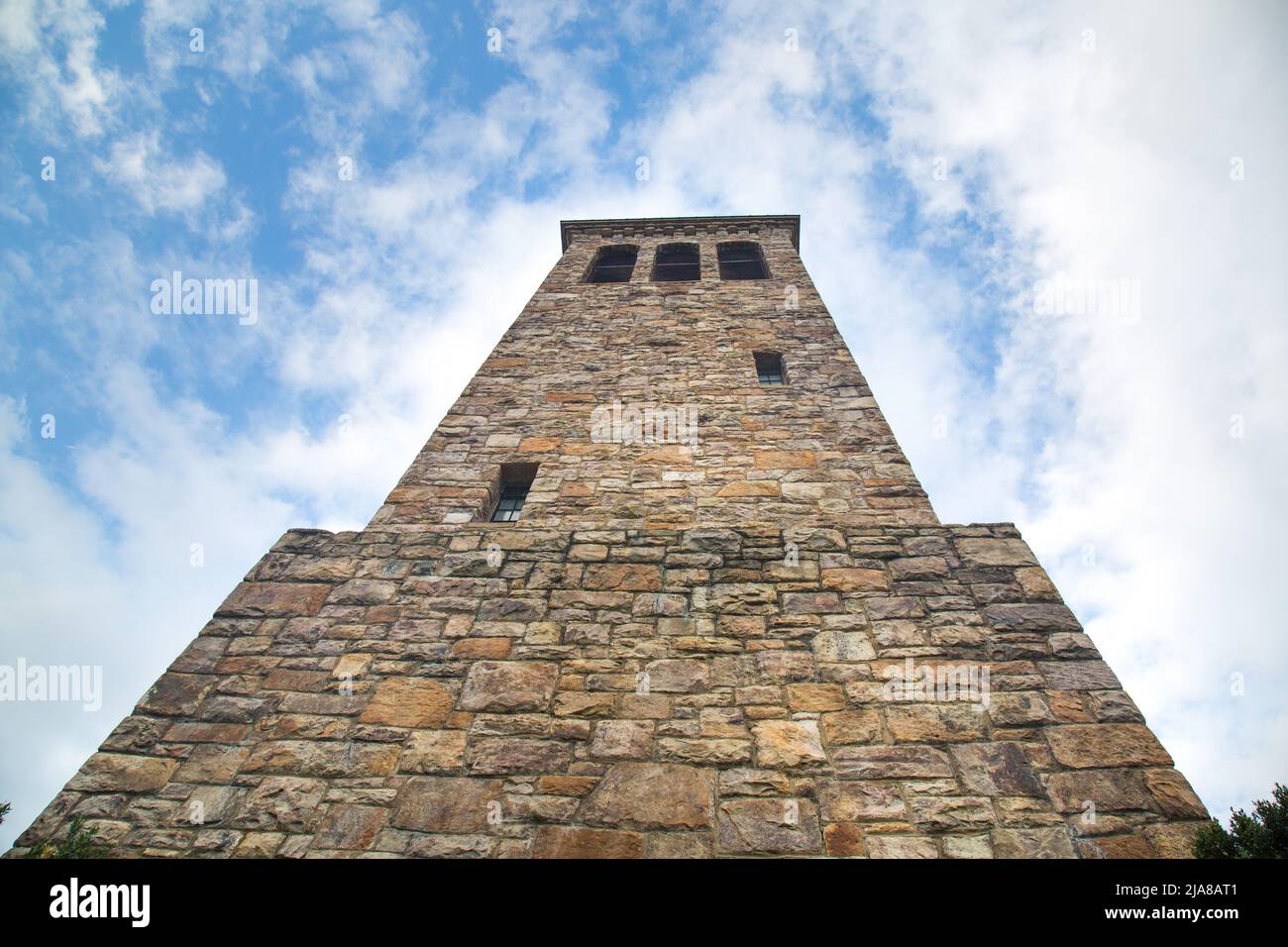 A stone tower with high windows stretches up into a blue sky with white ...