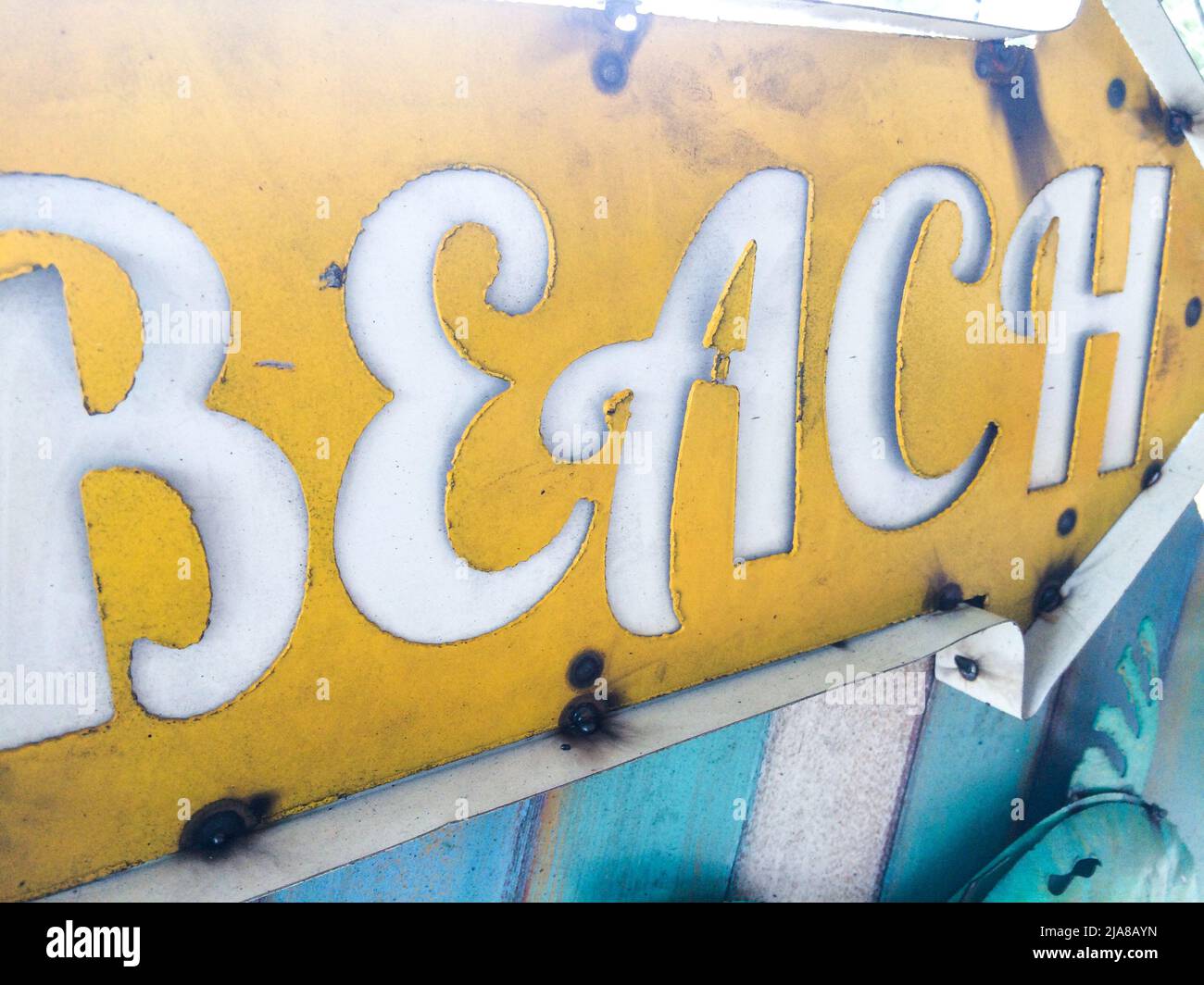 A well-worn and rusted metal arrow sign with the word BEACH punched out ...
