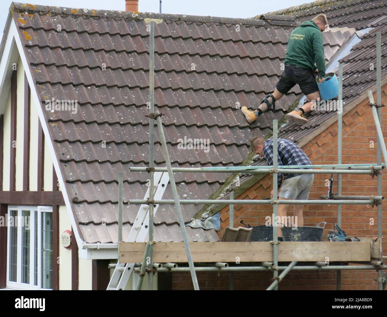 Working at height: workmen repair a house roof by climbing and kneeling ...
