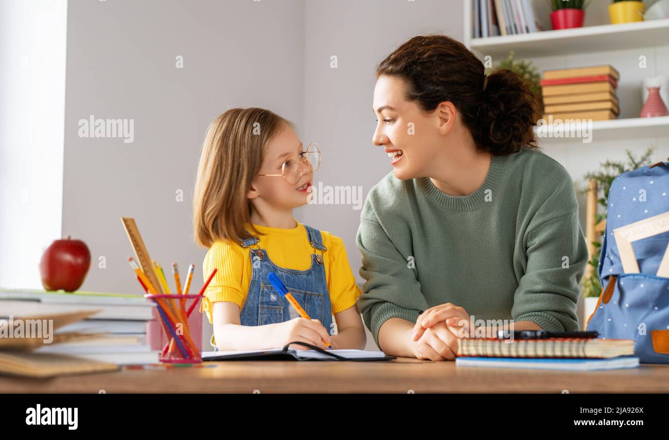Happy child and adult are sitting at desk. Girl doing homework or ...