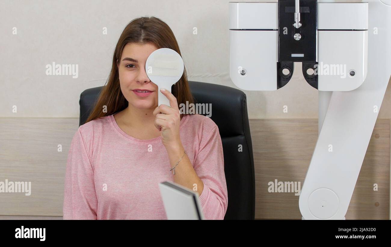 Ophthalmology treatment - young woman checking her visual acuity - closing her eye with an eye ...