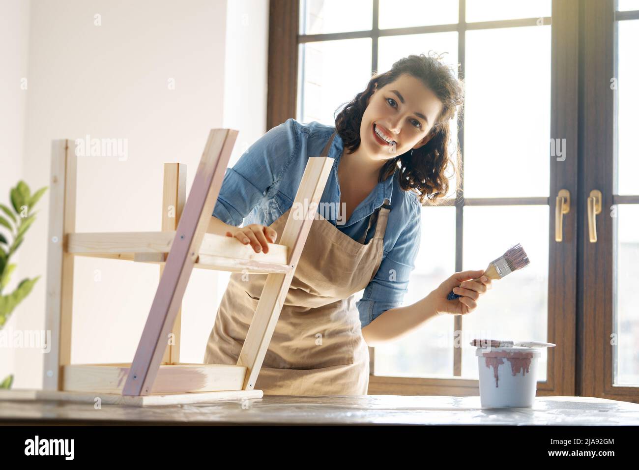 Happy woman is painting a wooden stepladder. Artisan is putting a ...
