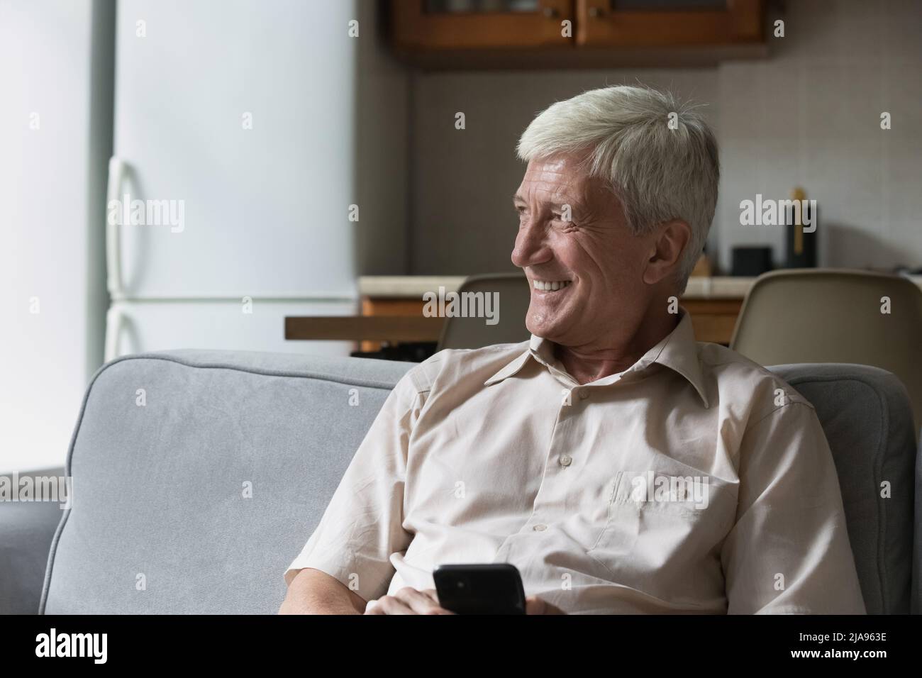 Smiling older age male pensioner sit on sofa hold smartphone Stock ...