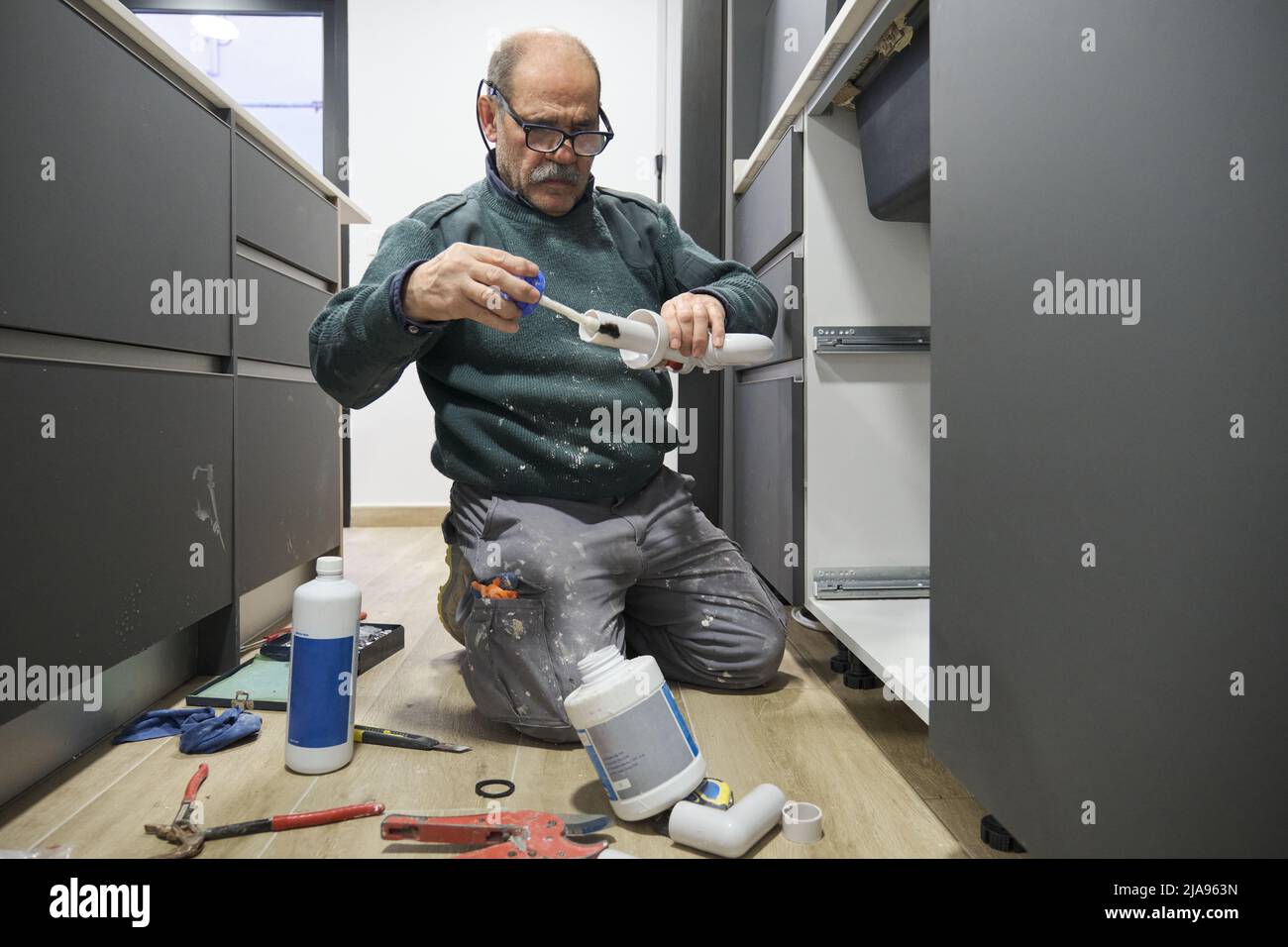 Mature plumber applying glue to a sink siphon white plastic pipe Stock ...