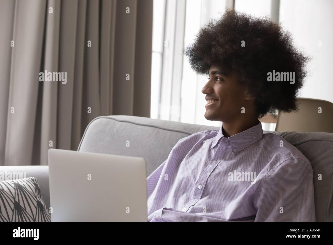 Happy dreamy Black laptop user sitting on couch, looking away Stock ...